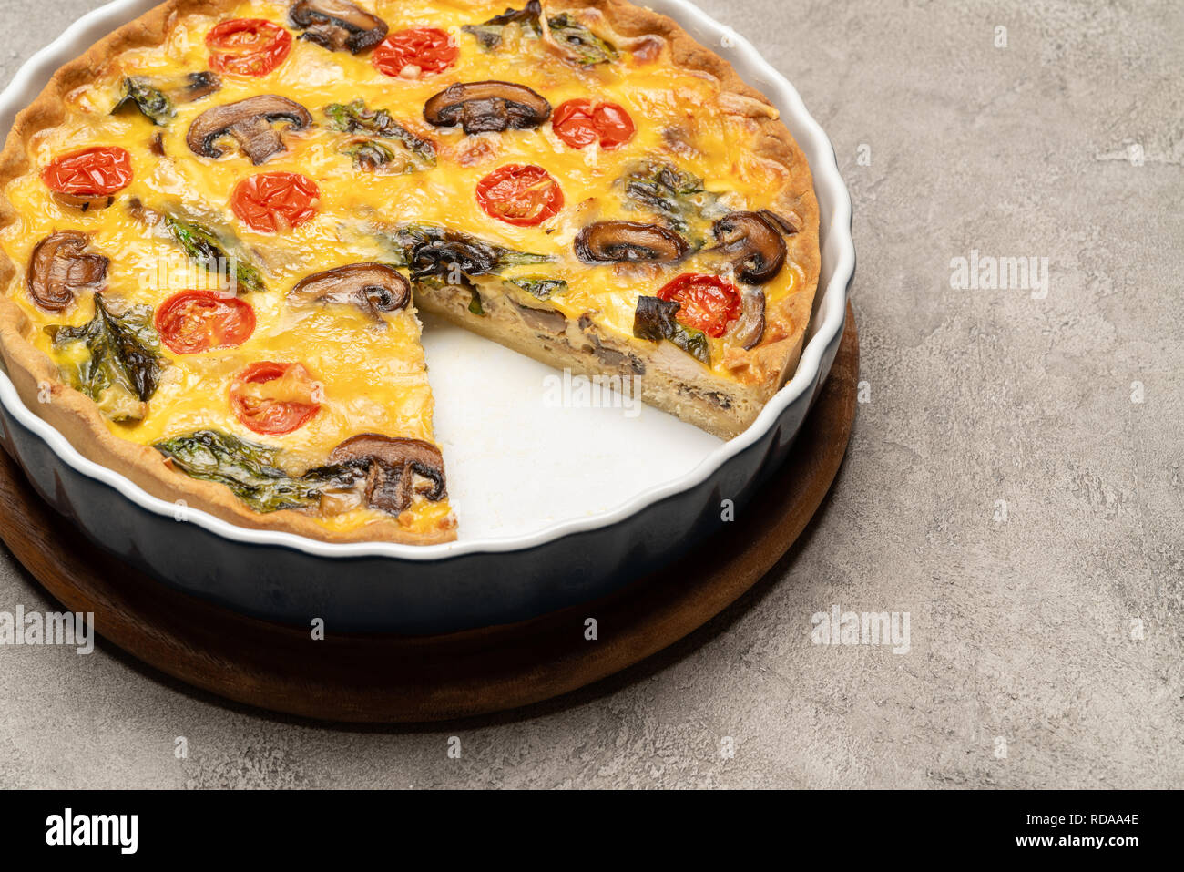 Baked homemade quiche pie in ceramic baking form on concrete background ...