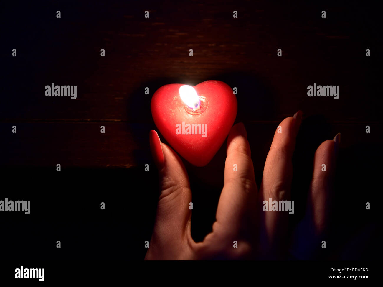 Women's hand holding a burning red candle in the dark light Stock Photo ...