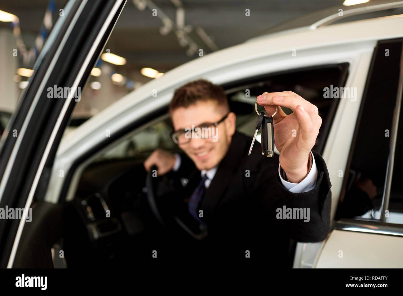 Man driver smiling holds car keys in car showroom Stock Photo - Alamy
