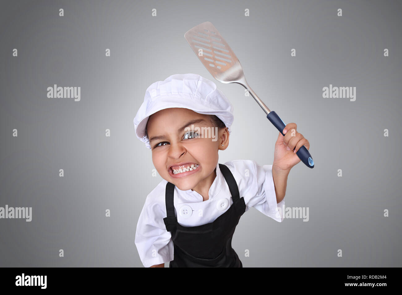 Angry little chef girl on a grey background Stock Photo - Alamy
