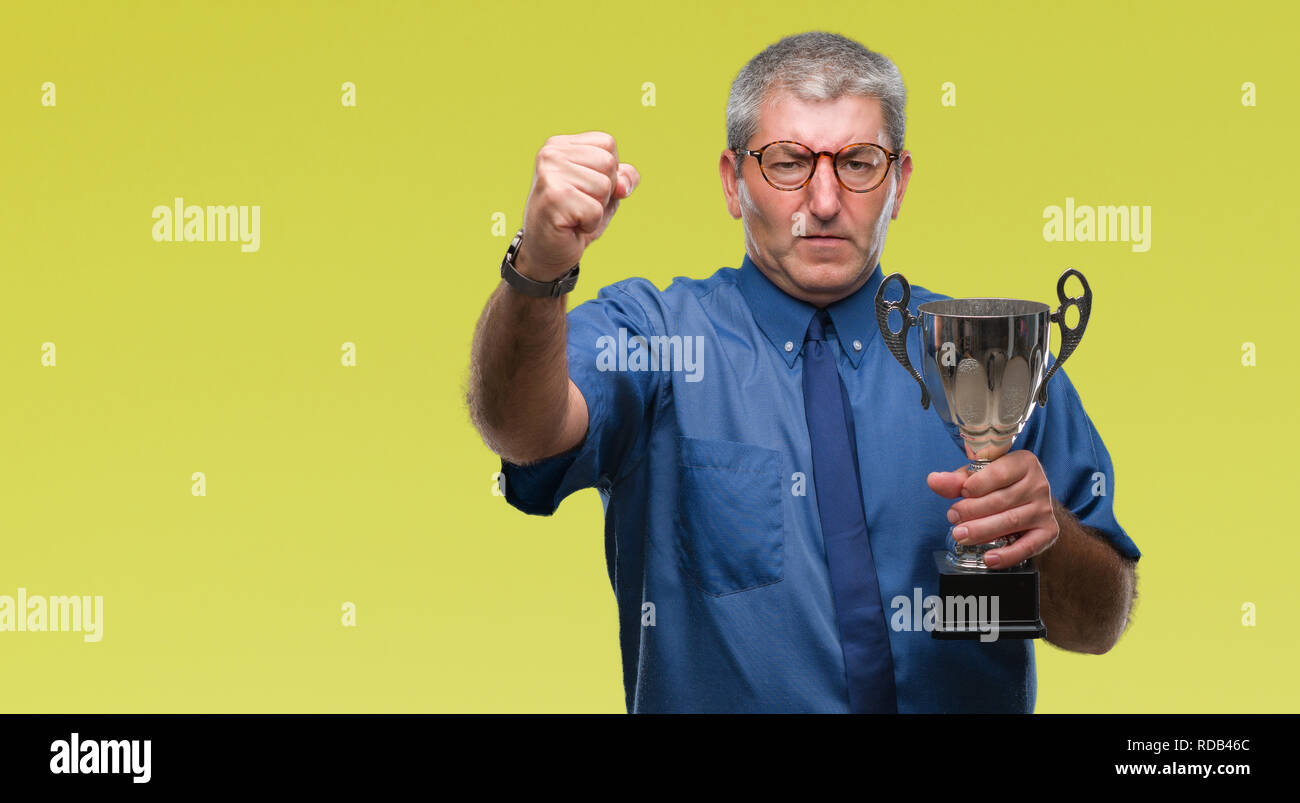 Handsome senior successful man holding trophy over isolated background ...