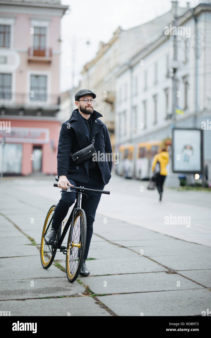 A young smiling stylish businessman pushing a bicycle while going to ...