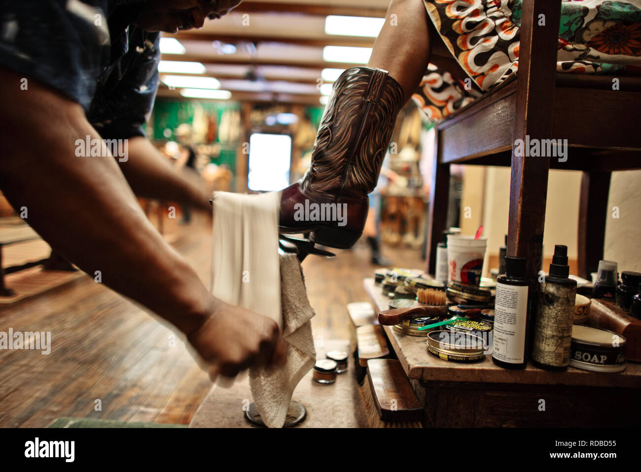 Shoeshiner rapidly polishes a customer's brown cowboy boots with a ...
