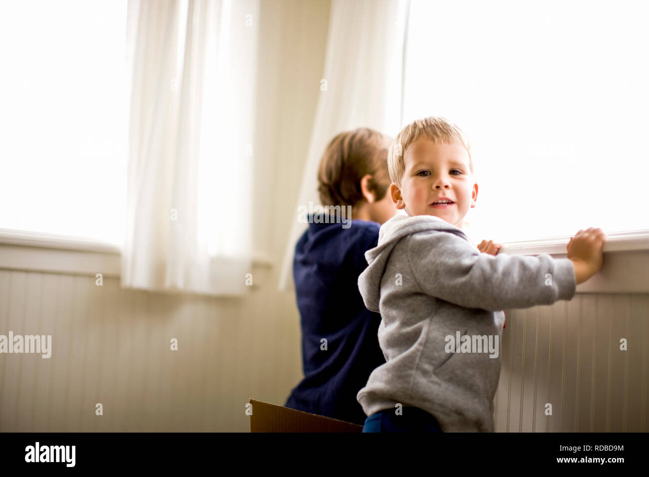 Two brothers looking out the window of their home Stock Photo - Alamy