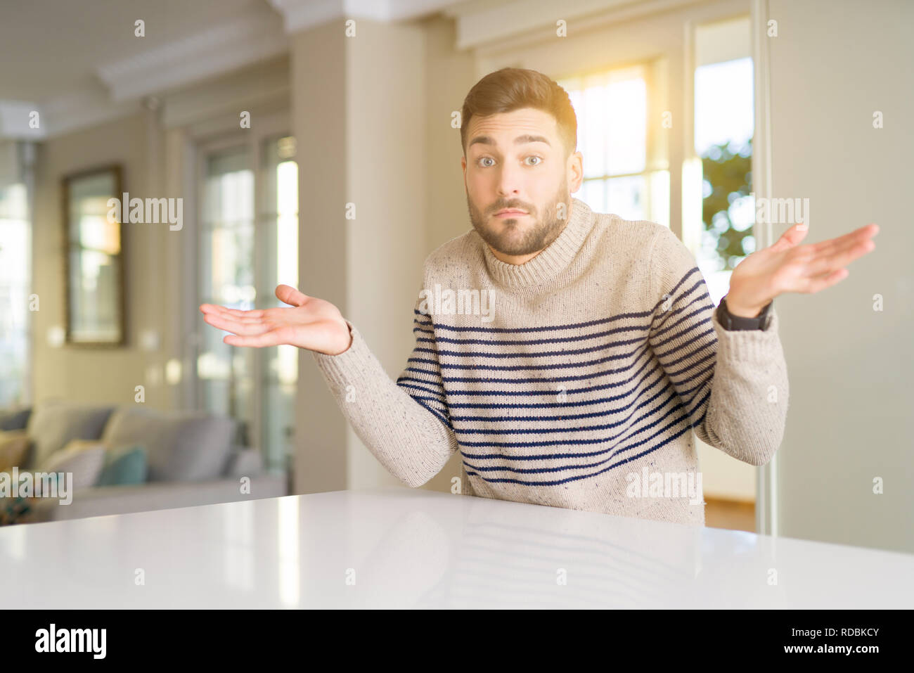 Young handsome man at home clueless and confused expression with arms ...