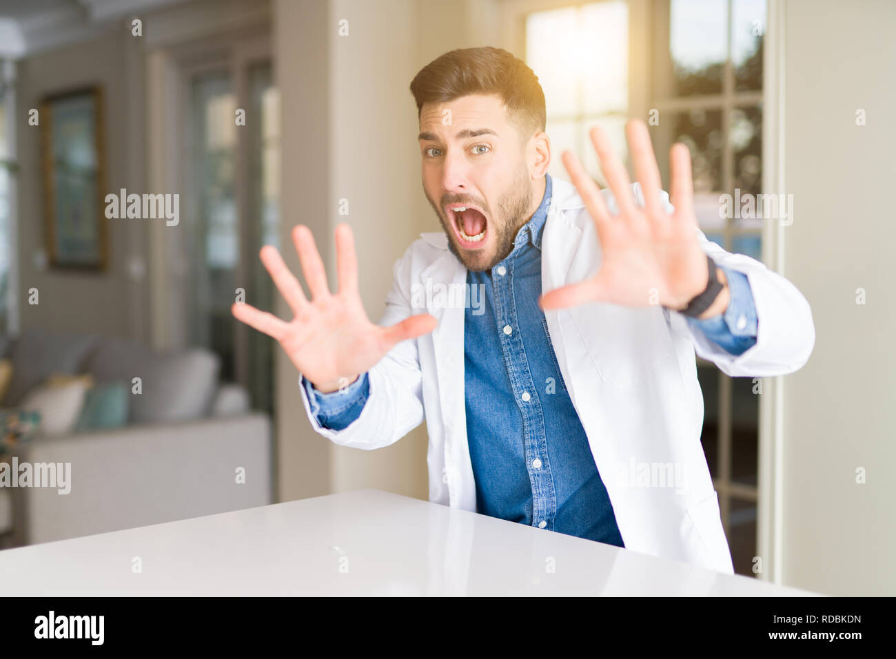 Young handsome doctor man at the clinic afraid and terrified with fear ...
