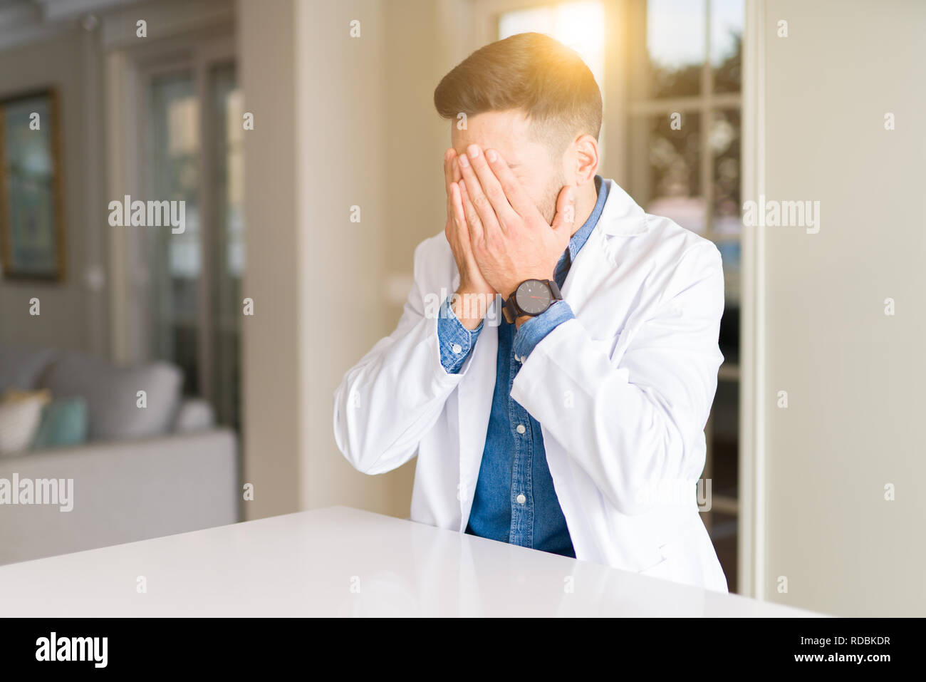Young handsome doctor man at the clinic with sad expression covering ...