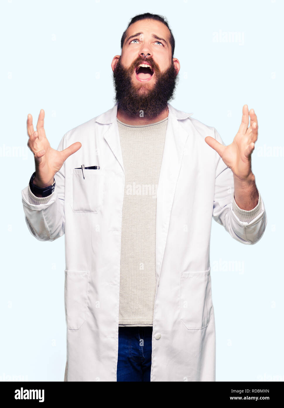 Young blond scientist man wearing white coat crazy and mad shouting and ...