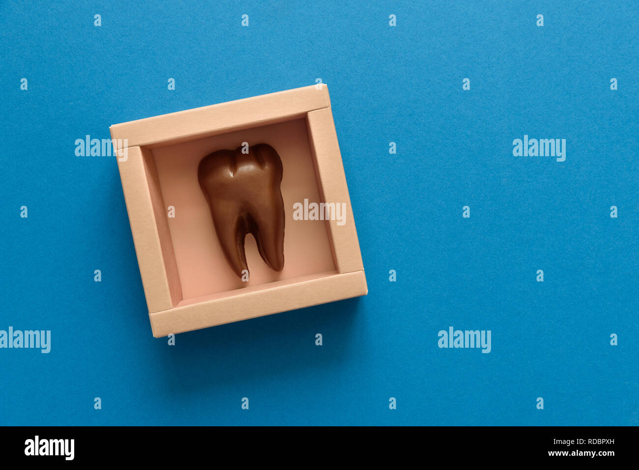 Tooth from chocolate in box on blue paper background. Top view. Copy ...