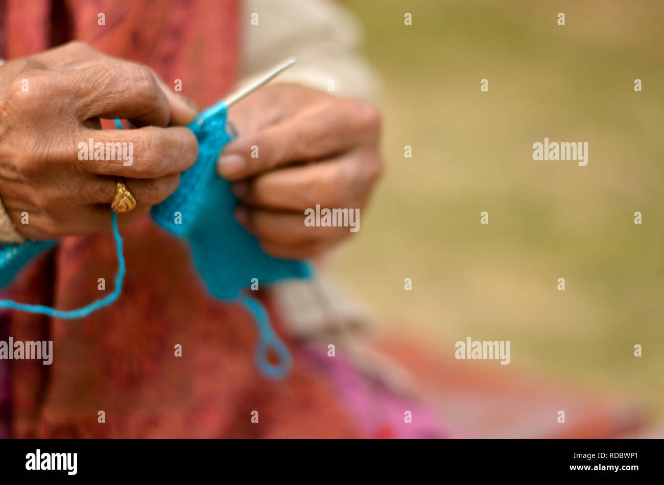 Close up of Indian woman knitting a blue sweater on a park bench in ...