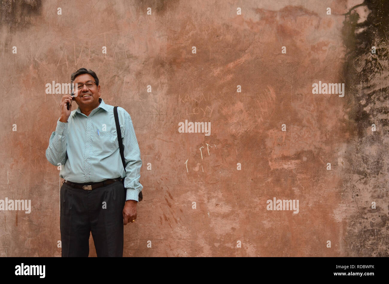 Senior Indian man smiling and speaking on phone standing against brown ...