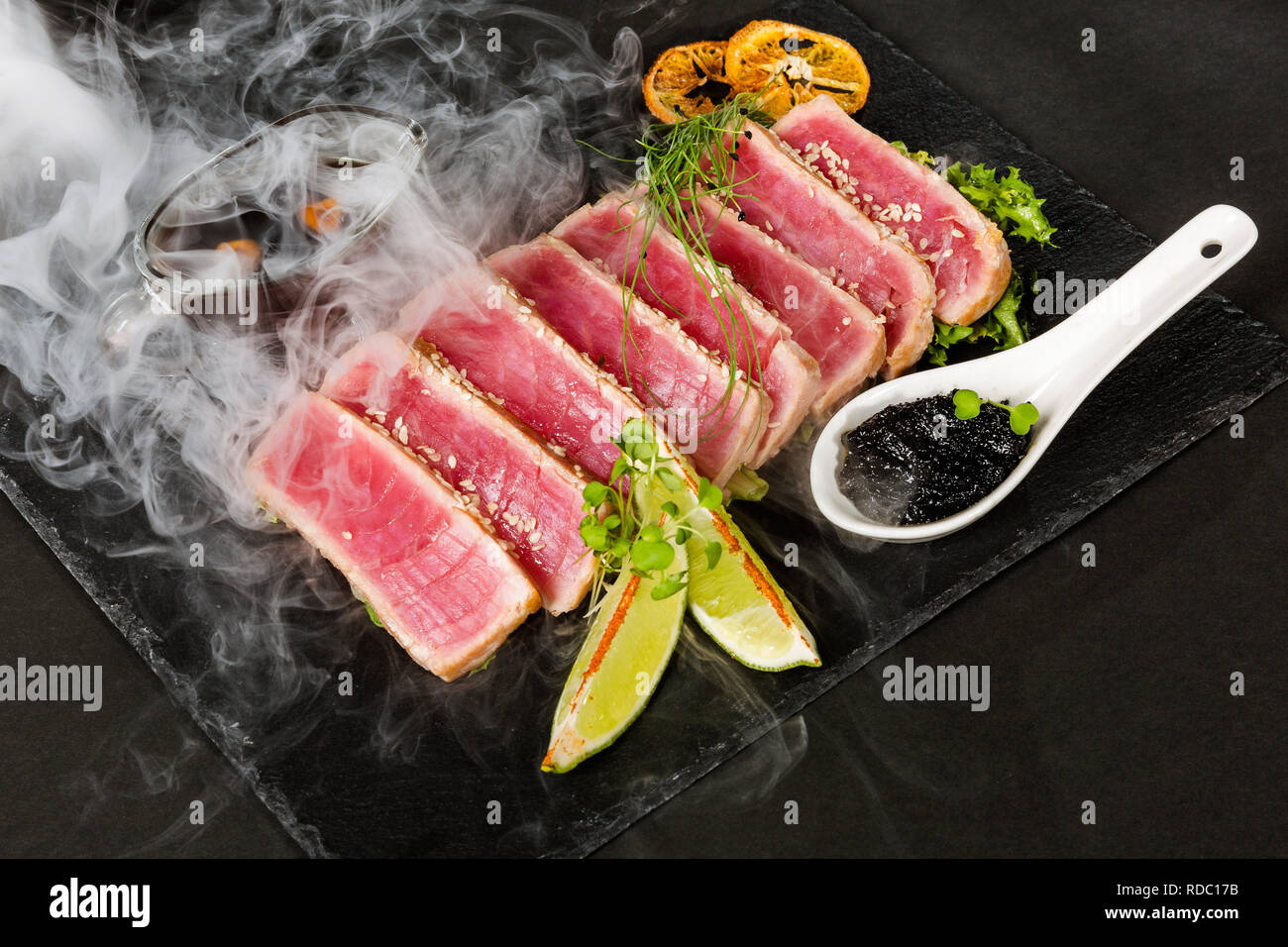 Sliced tuna steak with lime and sesame in puffs of white smoke Stock ...