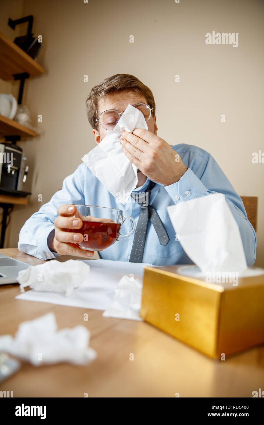 Sick man with handkerchief sneezing blowing nose while working in ...