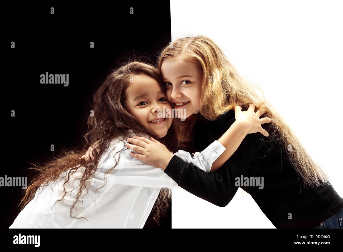 The portrait of two hugging embracing happy girls on a white and black ...