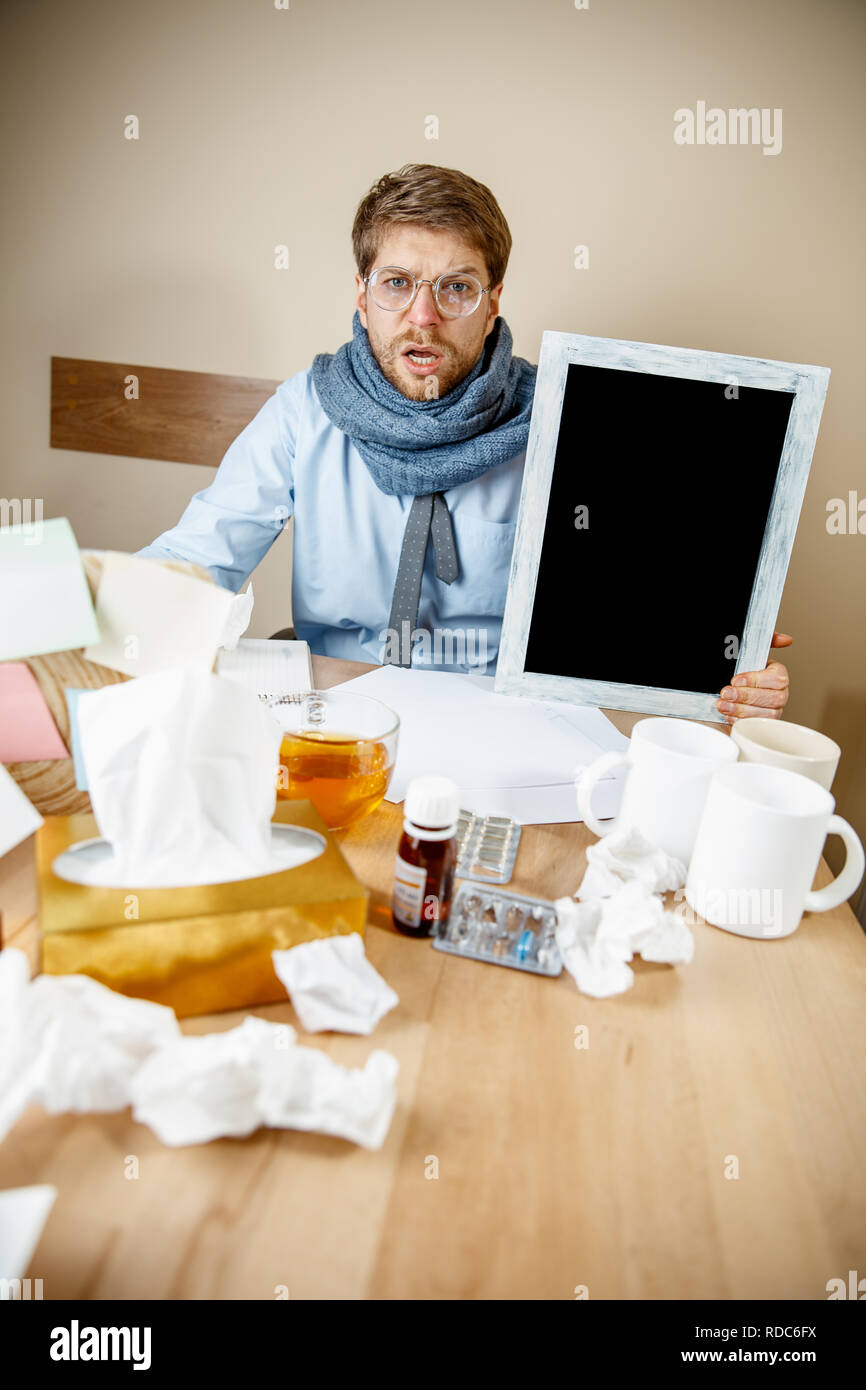 Sick man with empty poster for copyspace while working in office ...