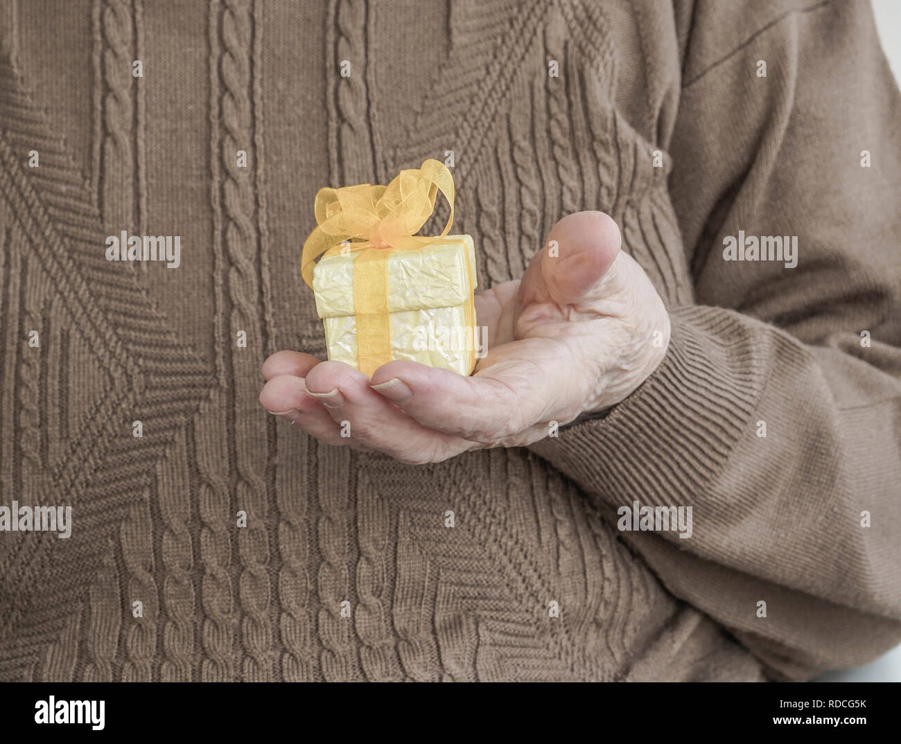 A small yellow gift on wrinkled palm of a senior person Stock Photo - Alamy