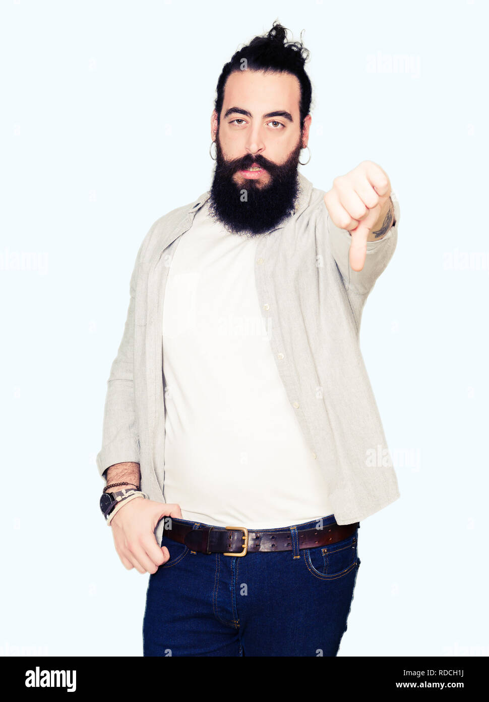 Young man with long hair, beard and earrings looking unhappy and angry ...