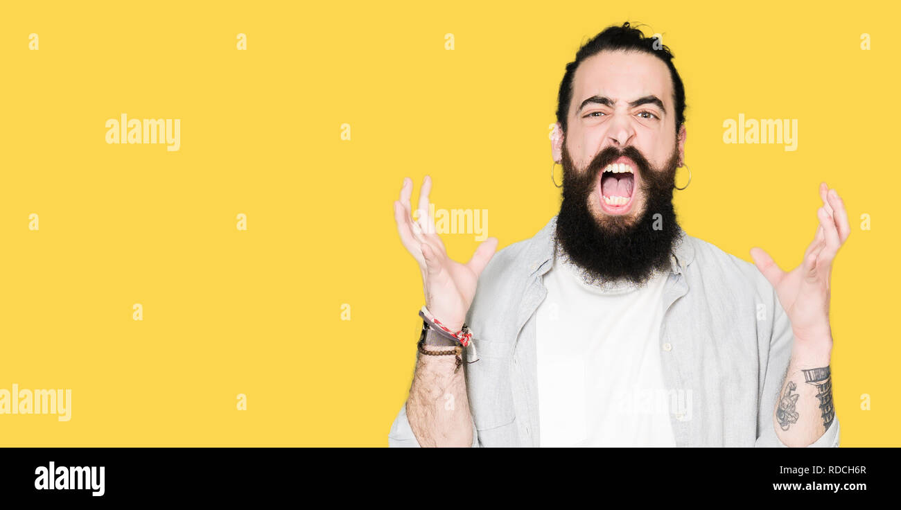 Young man with long hair, beard and earrings crazy and mad shouting and ...