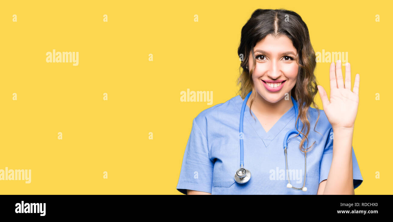 Young adult doctor woman wearing medical uniform Waiving saying hello ...