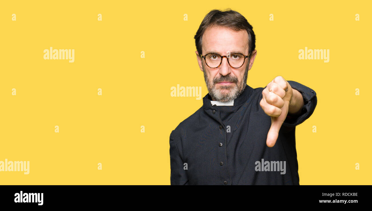 Middle age priest man wearing catholic robe looking unhappy and angry ...