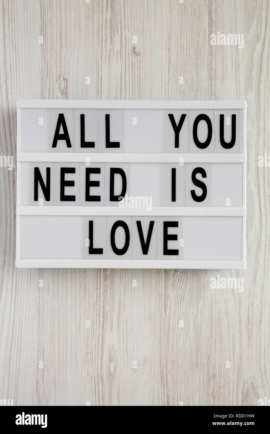 Modern board with text 'All you need is love' on a white wooden background, top view. From above ...