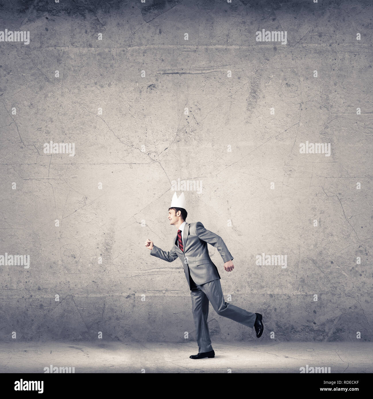 Young handsome businessman wearing white paper crown running in a hurry ...