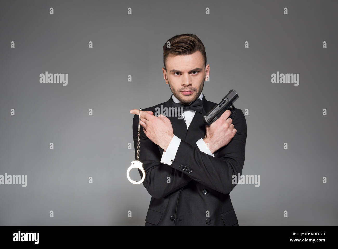 serious secret agent in black tuxedo holding gun and handcuffs ...