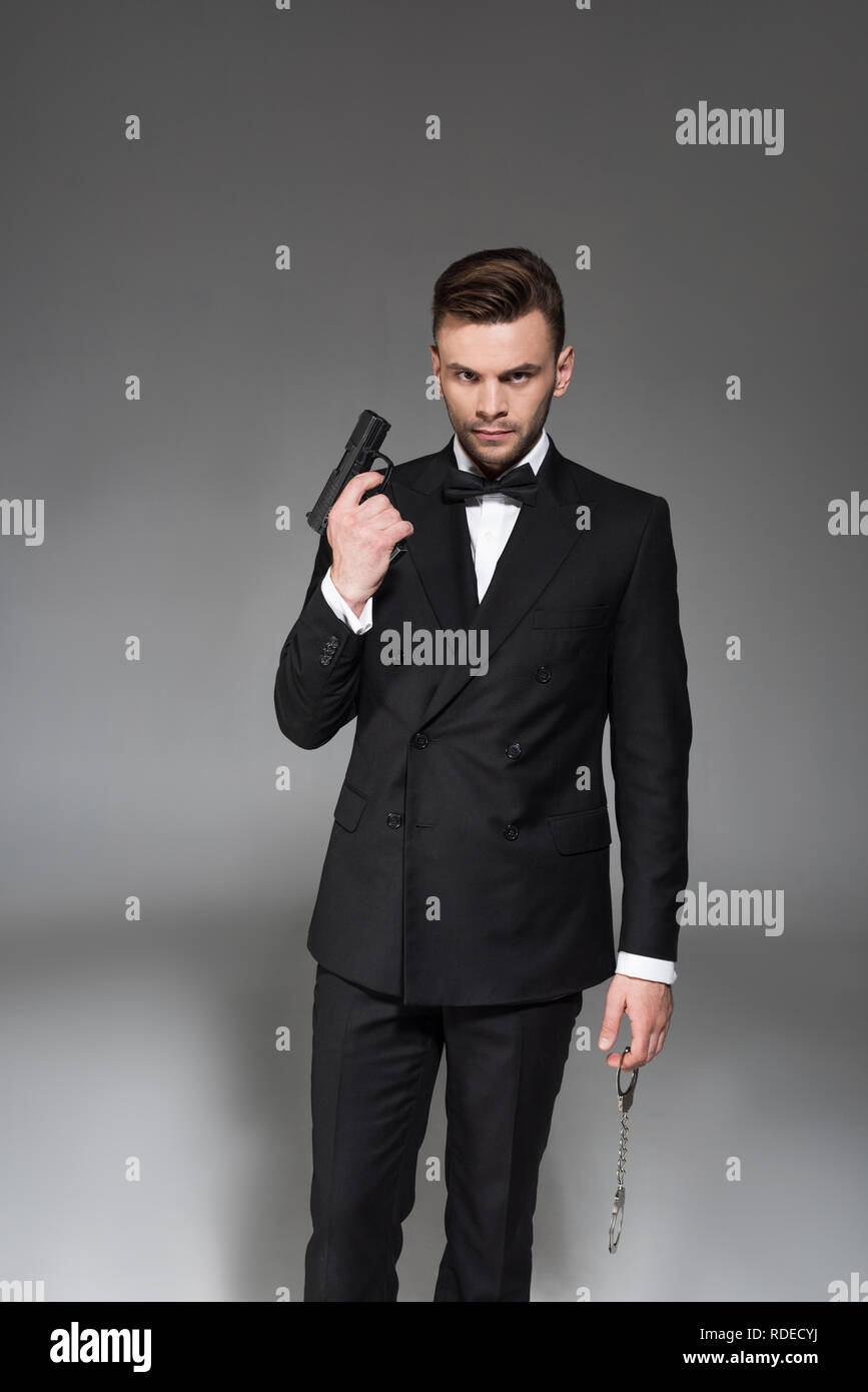 handsome secret agent in tuxedo holding handgun and handcuffs, isolated ...