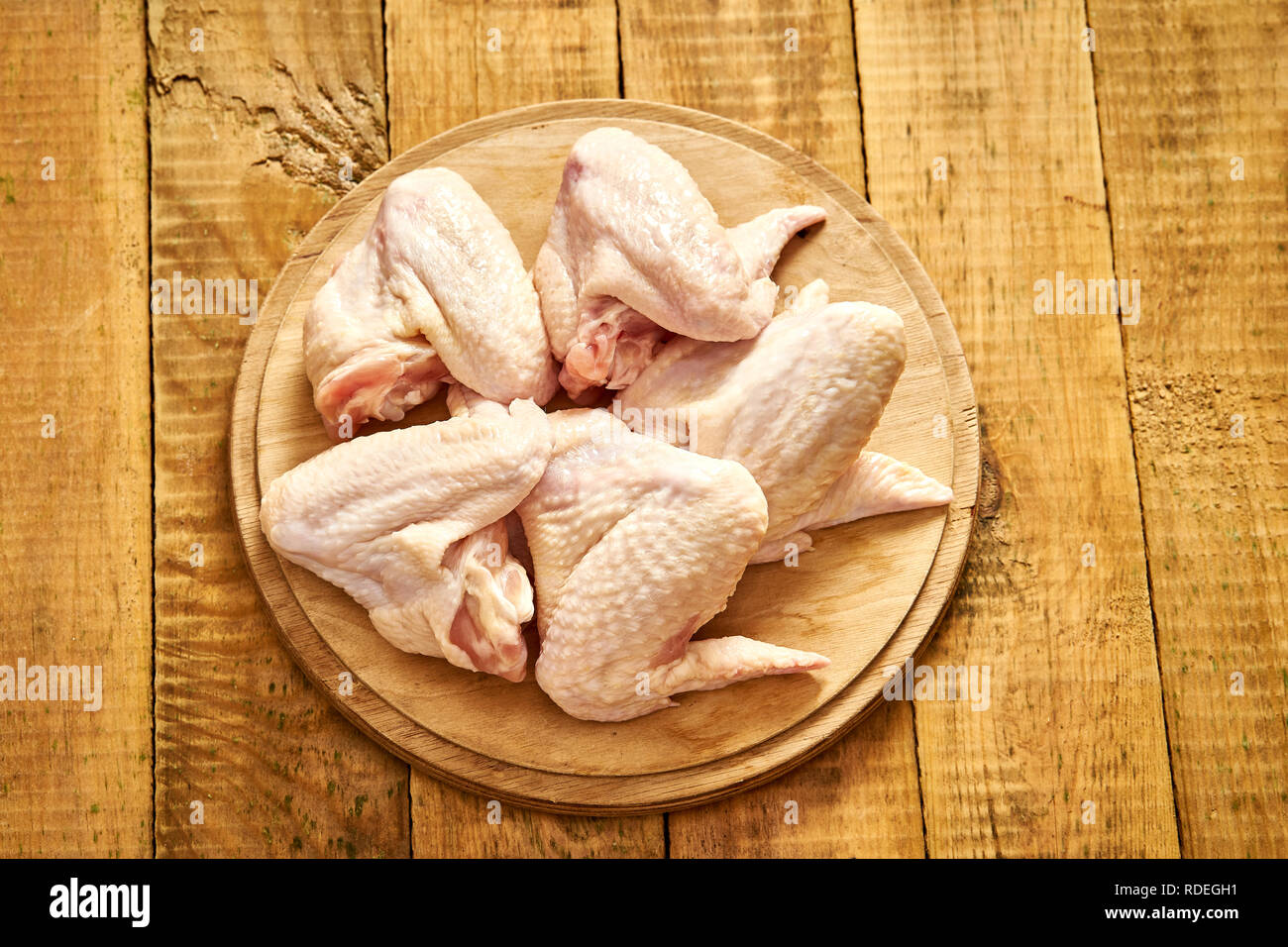 Fresh organic chicken wings on round chopping board on old wooden table ...