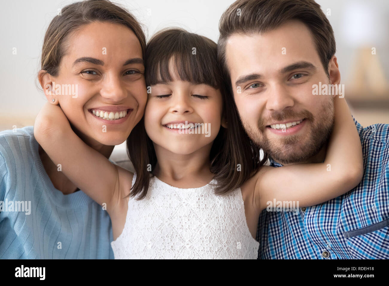 Cute little daughter embracing parents mom and dad, headshot por Stock ...