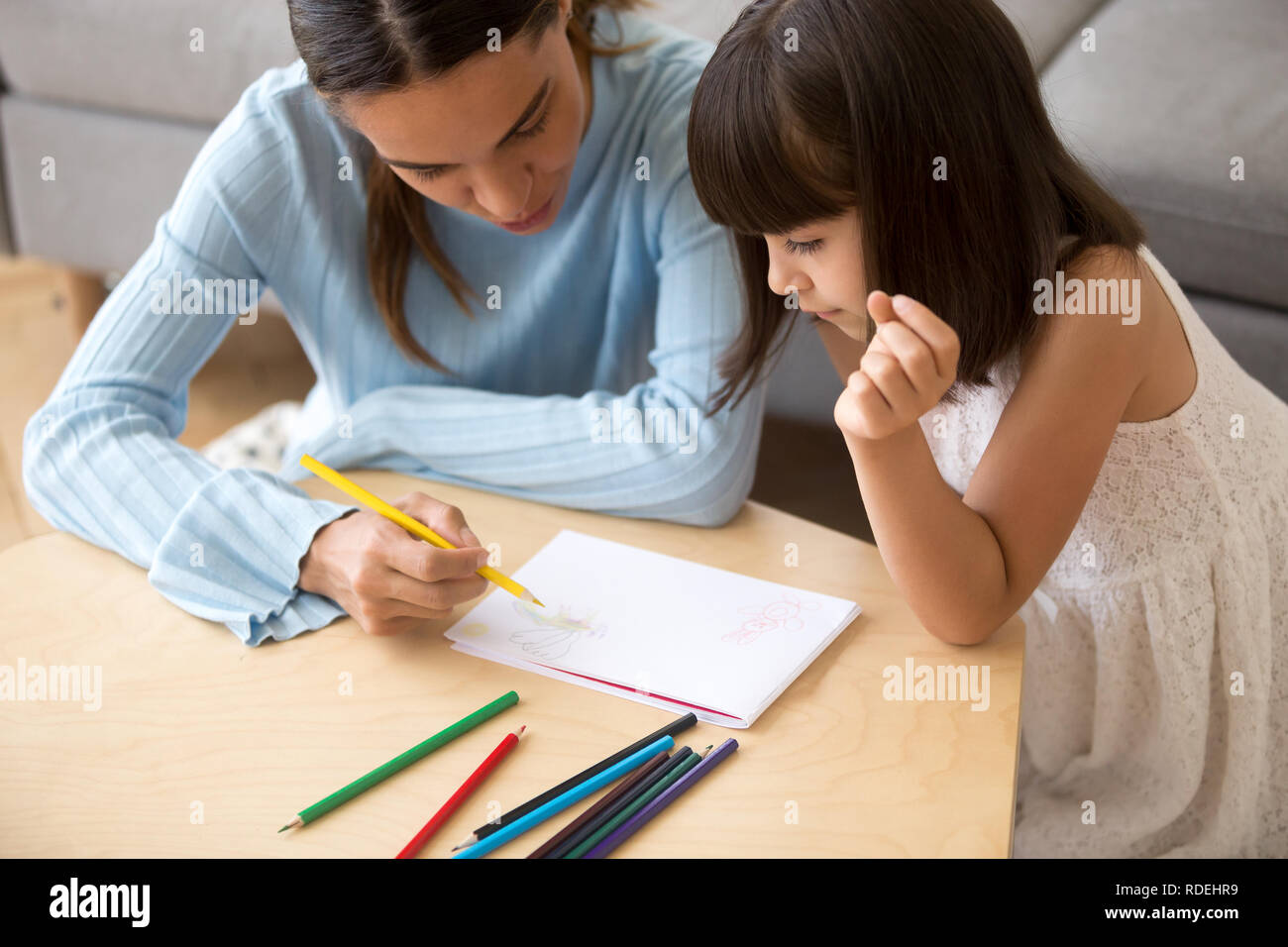 Focused mom holding colored pencil teaching kid daughter to draw Stock ...