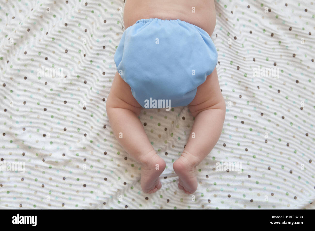 Baby wearing a blue cloth diaper laying on their belly on a polka ...