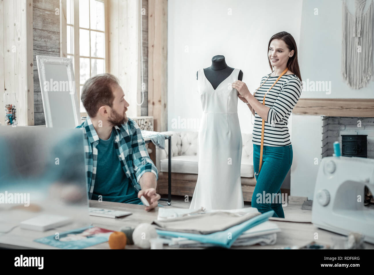 Dark-haired designer standing near dress form with white long dress ...