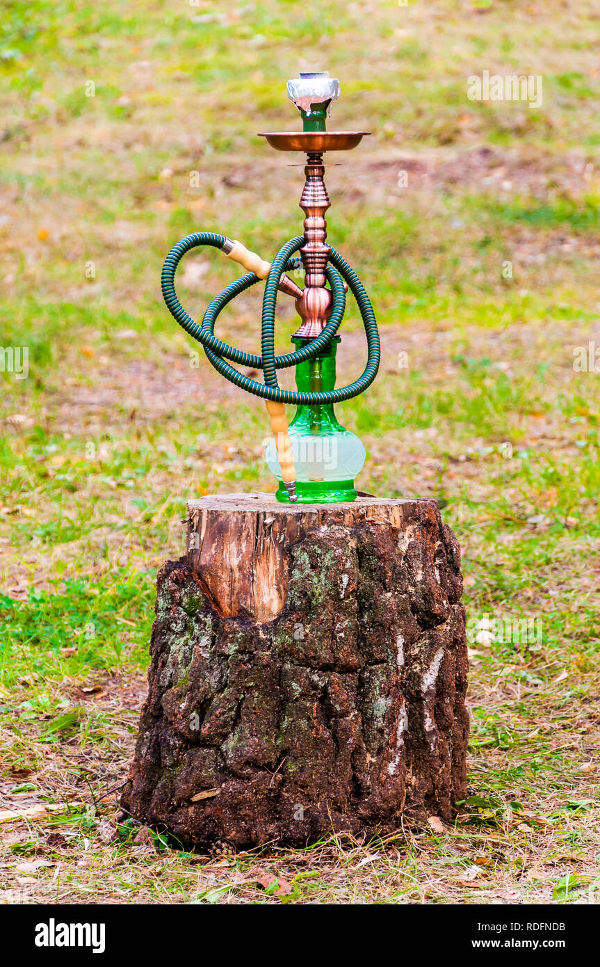 Green glass and copper metal hookah with twisted elastic hose standing ...