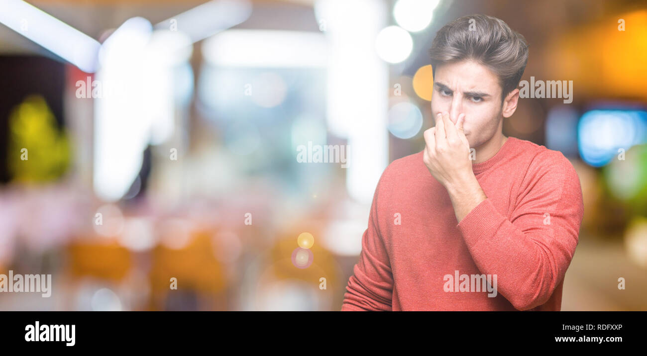 Young handsome man over isolated background smelling something stinky ...
