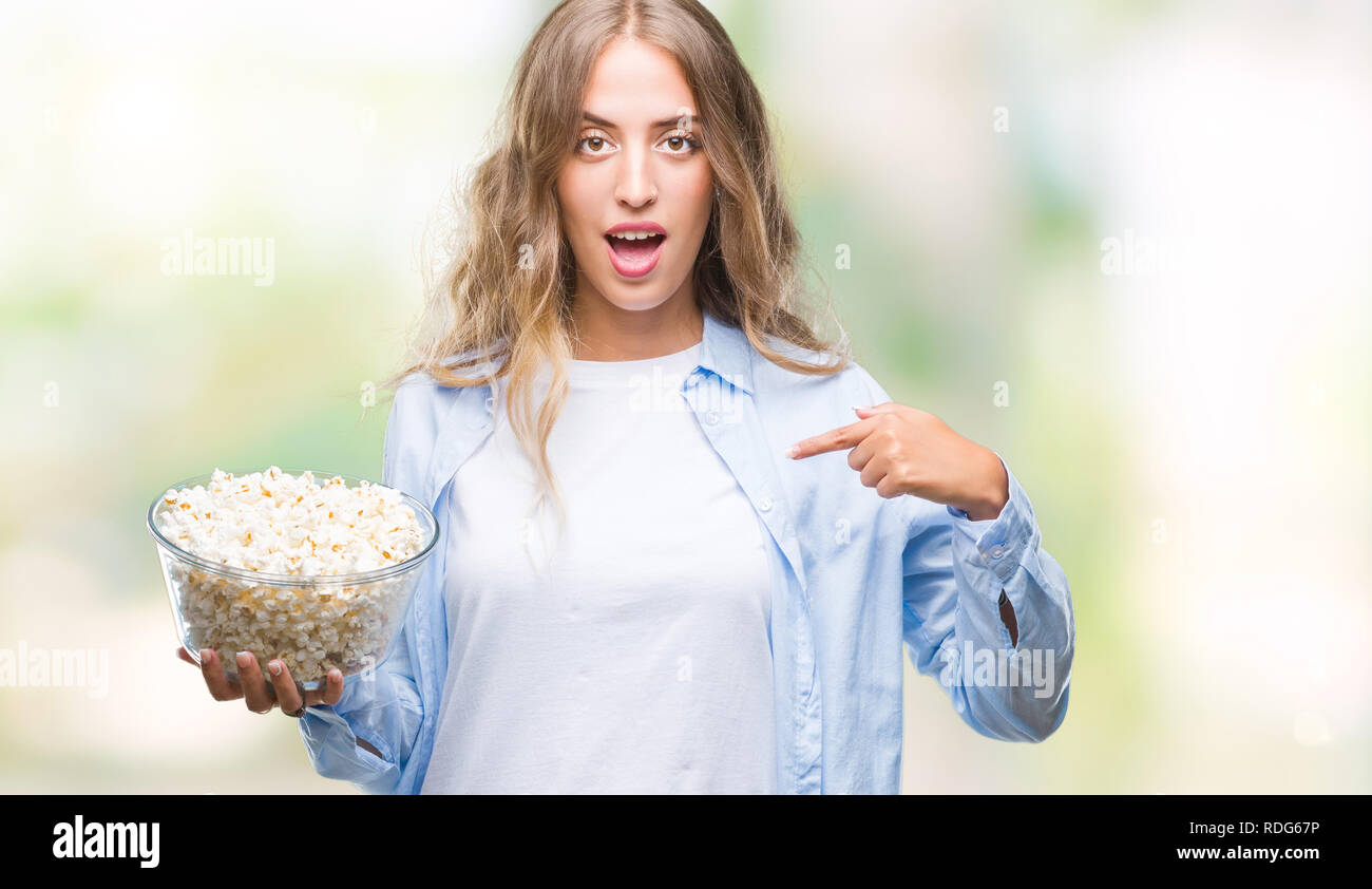 Beautiful young blonde woman eating popcorn over isolated background ...