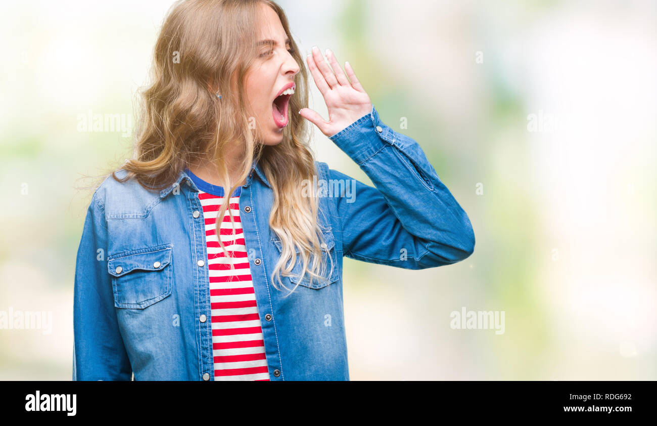 Beautiful young blonde woman over isolated background shouting and ...