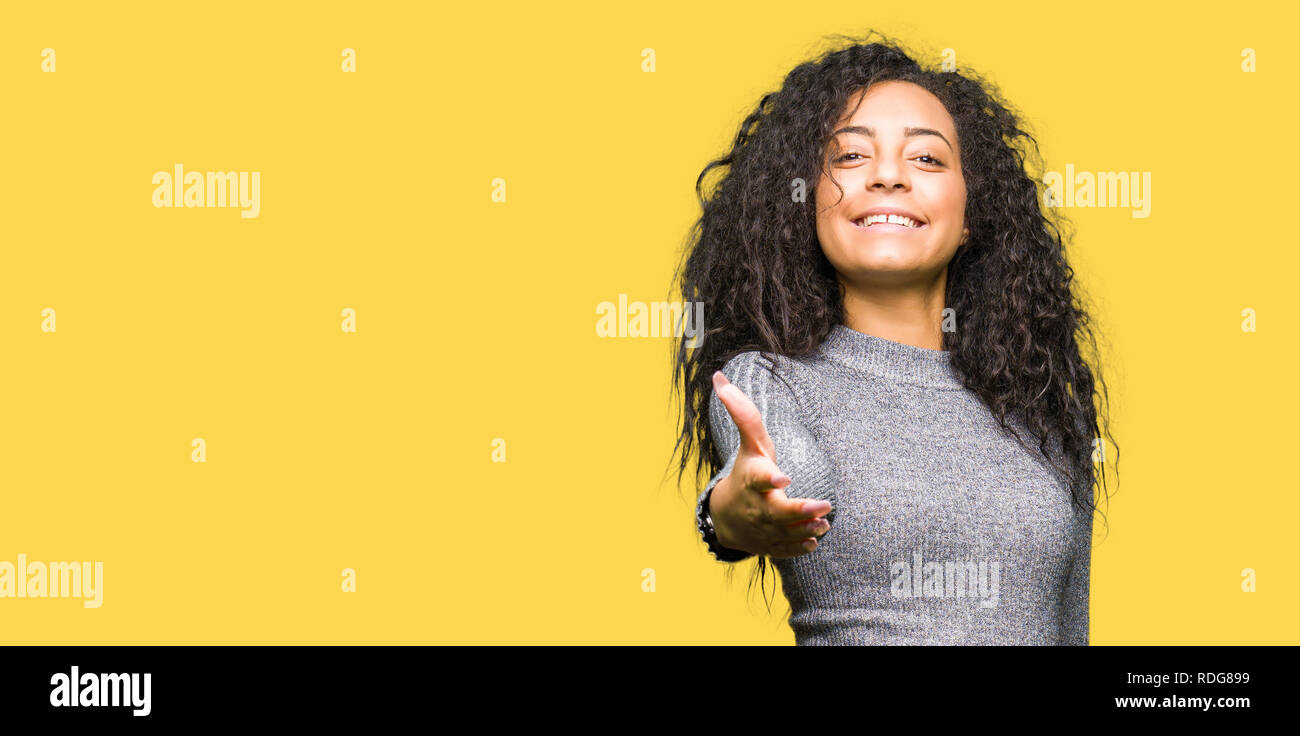 Young beautiful girl with curly hair smiling friendly offering ...