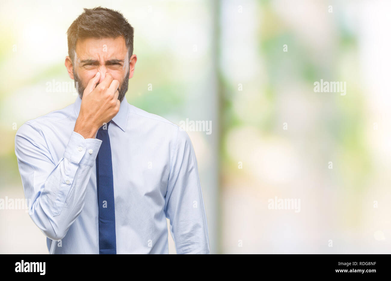 Adult hispanic business man over isolated background smelling something ...