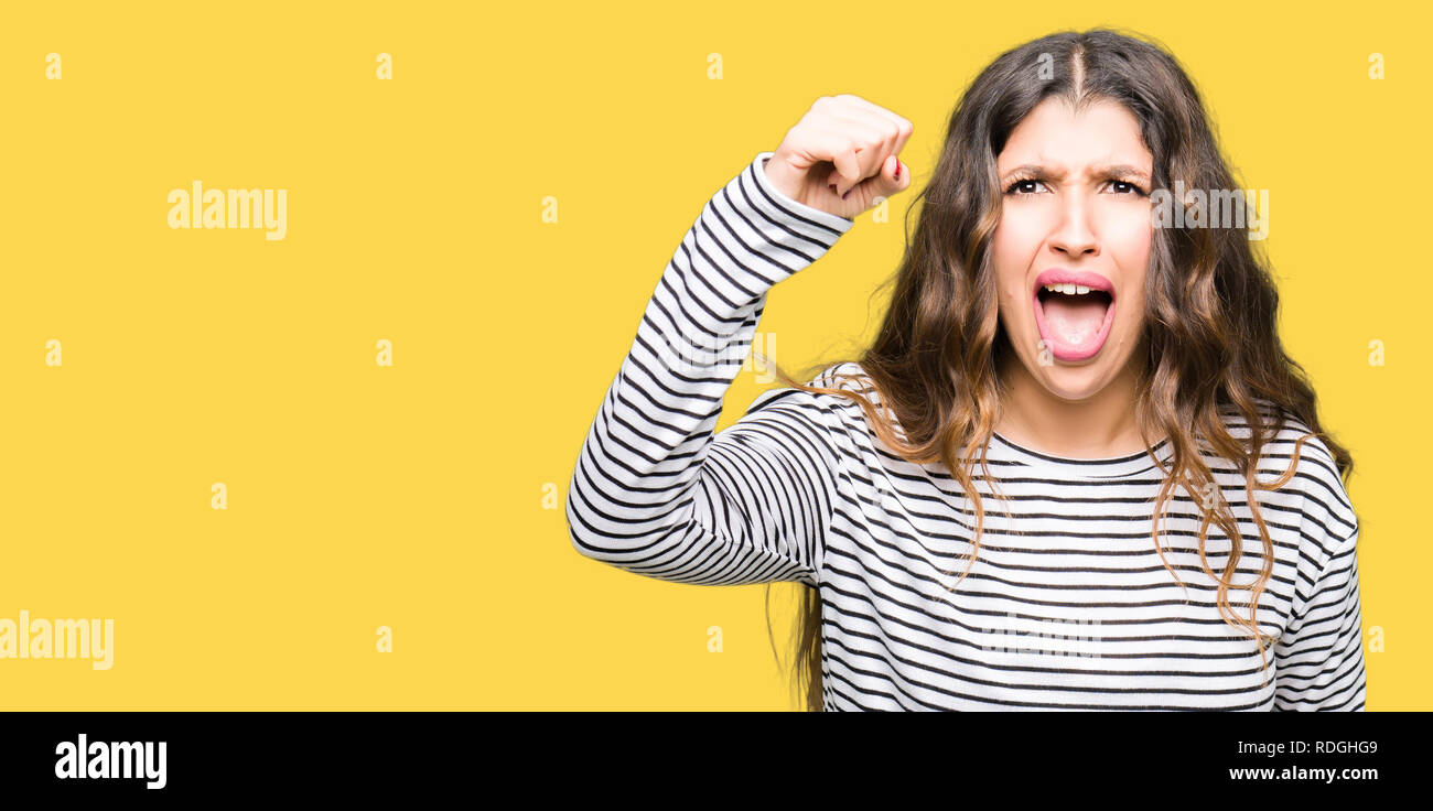 Young beautiful woman wearing stripes sweater angry and mad raising ...