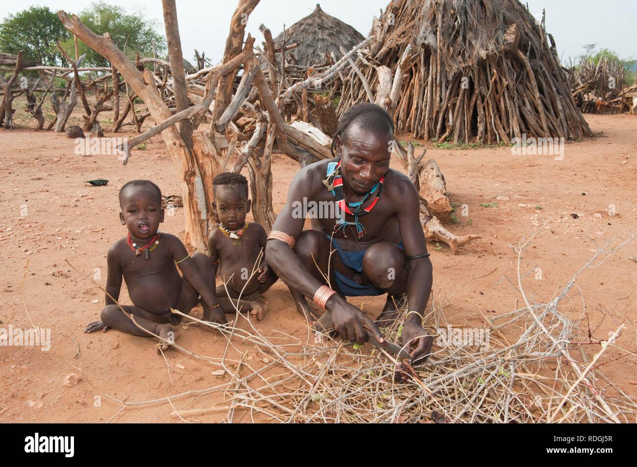 Hamar man with two little children cutting meat in the village, Omo ...
