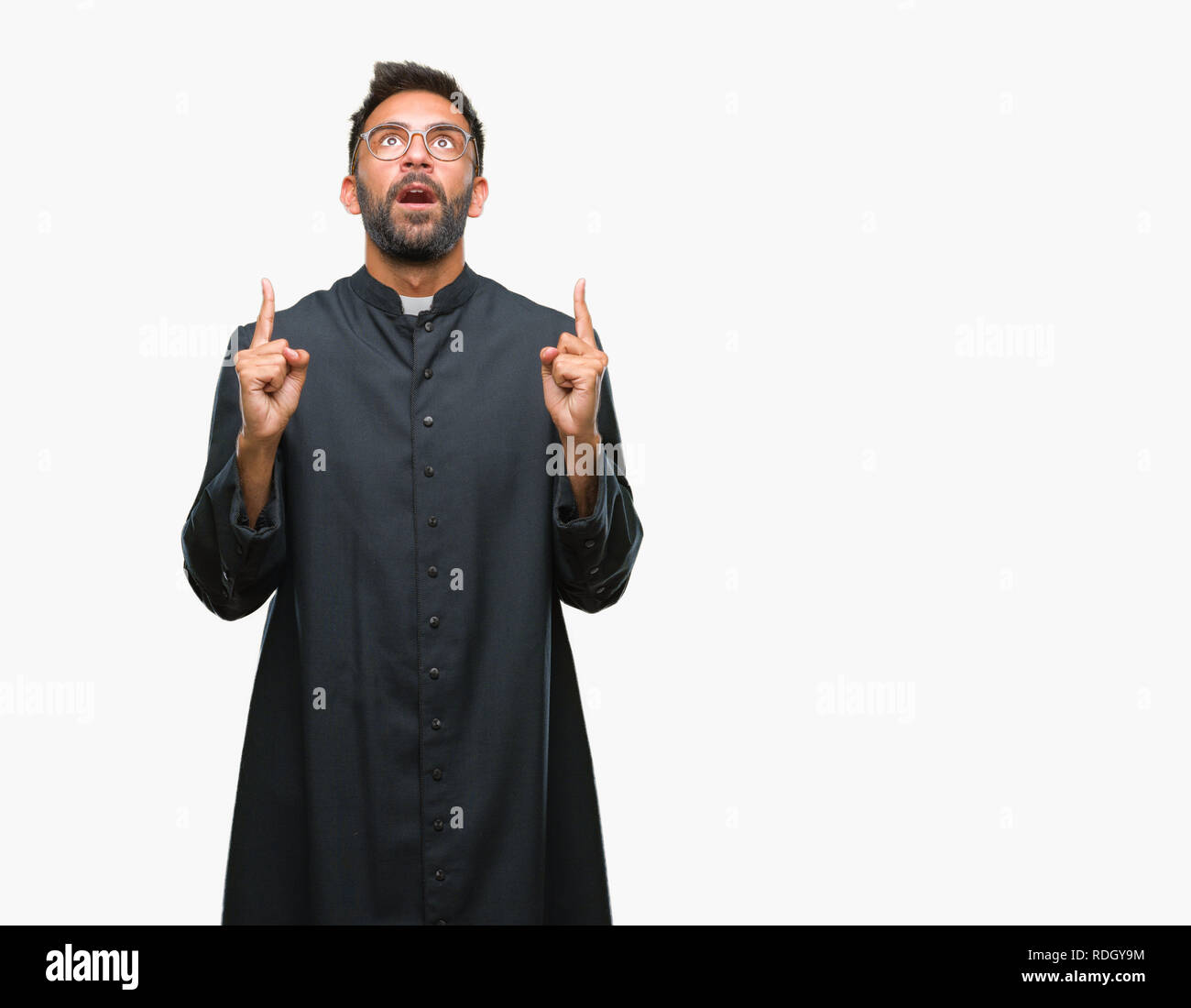 Adult hispanic catholic priest man over isolated background amazed and ...