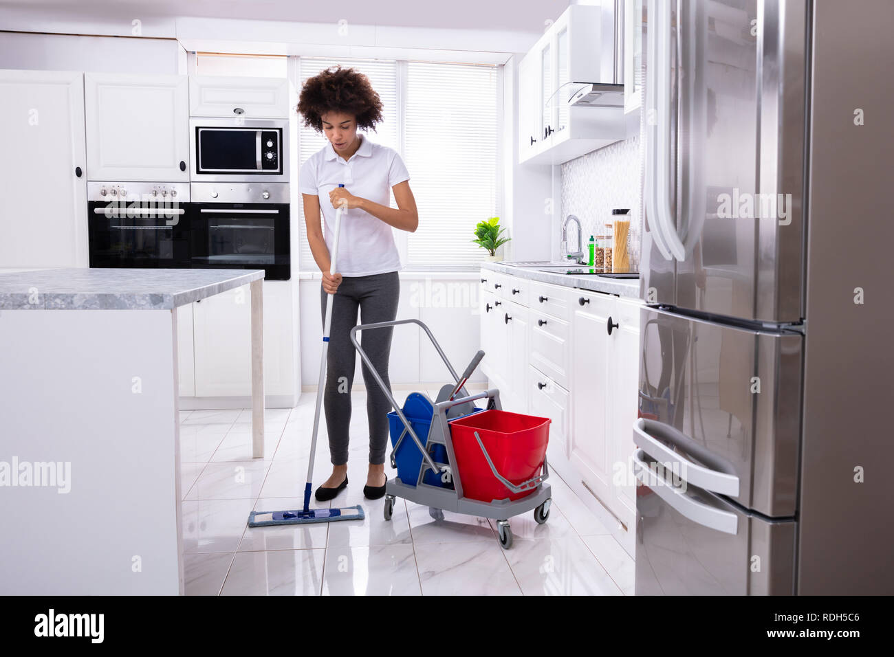Female Janitor Cleaning The White Floor With Mop In Modern Kitchen ...