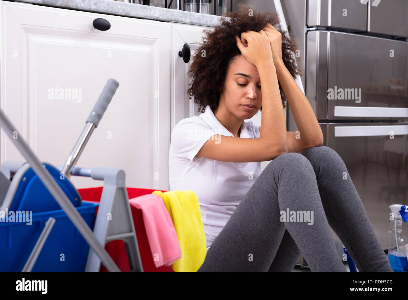 Exhausted African Young Woman Sitting On Floor In The Kitchen Stock ...