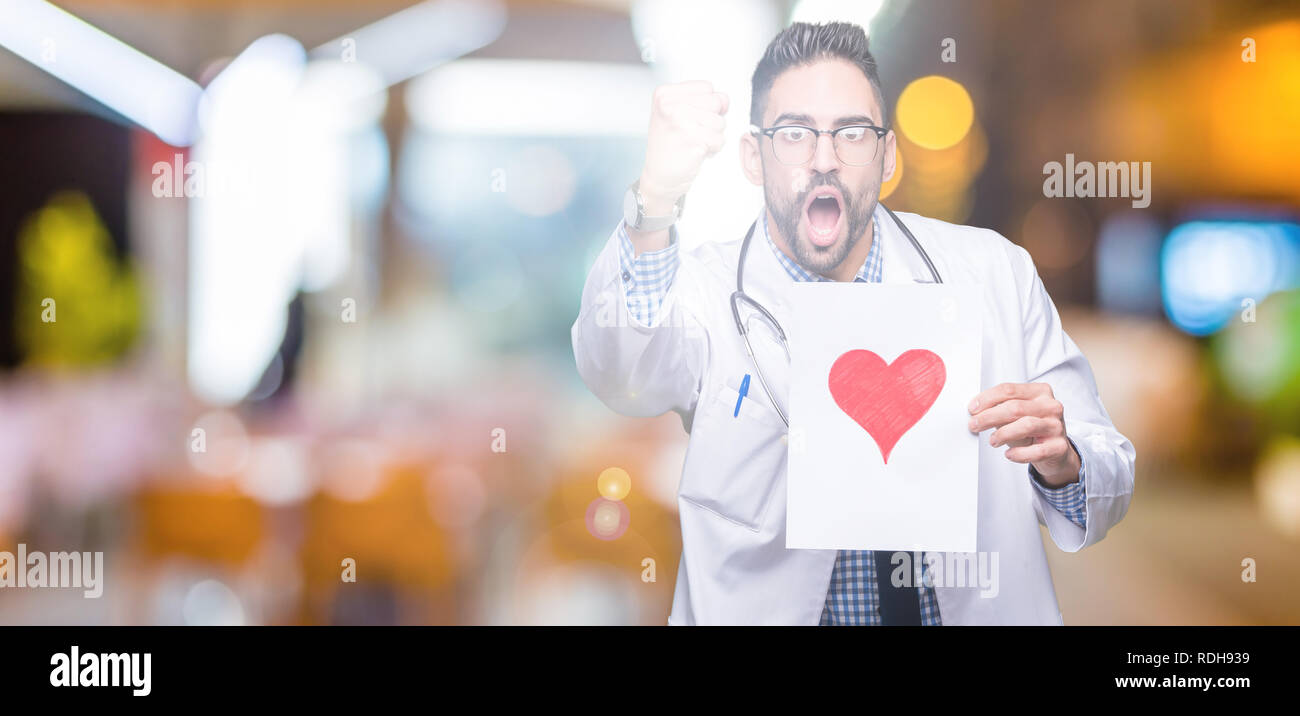 Handsome young doctor man holding paper with red heart over isolated ...