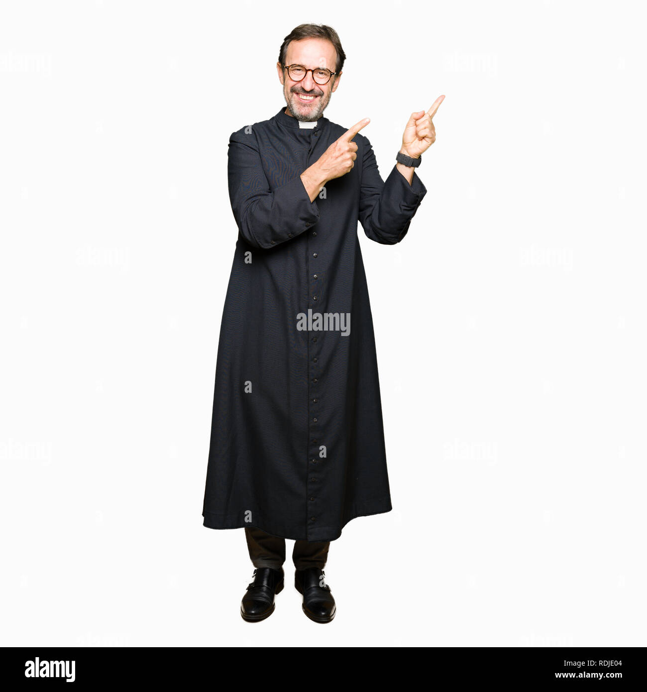 Middle age priest man wearing catholic robe smiling and looking at the ...