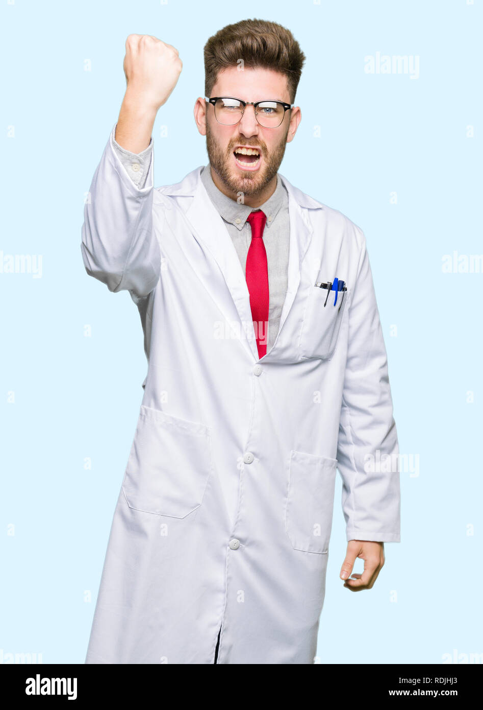Young handsome scientist man wearing glasses angry and mad raising fist ...