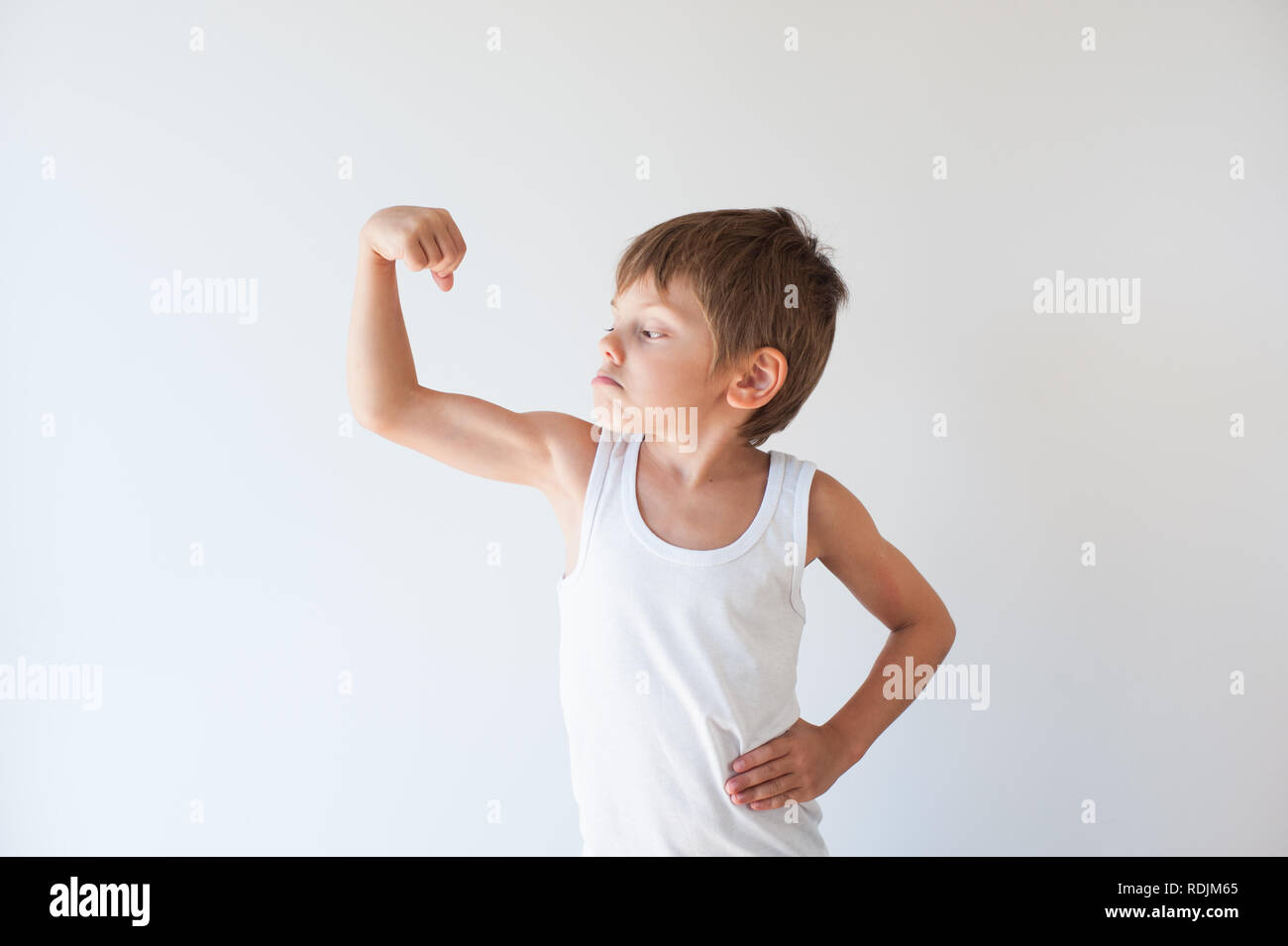 strong small child in tank top showing his muscle with grimace on his ...