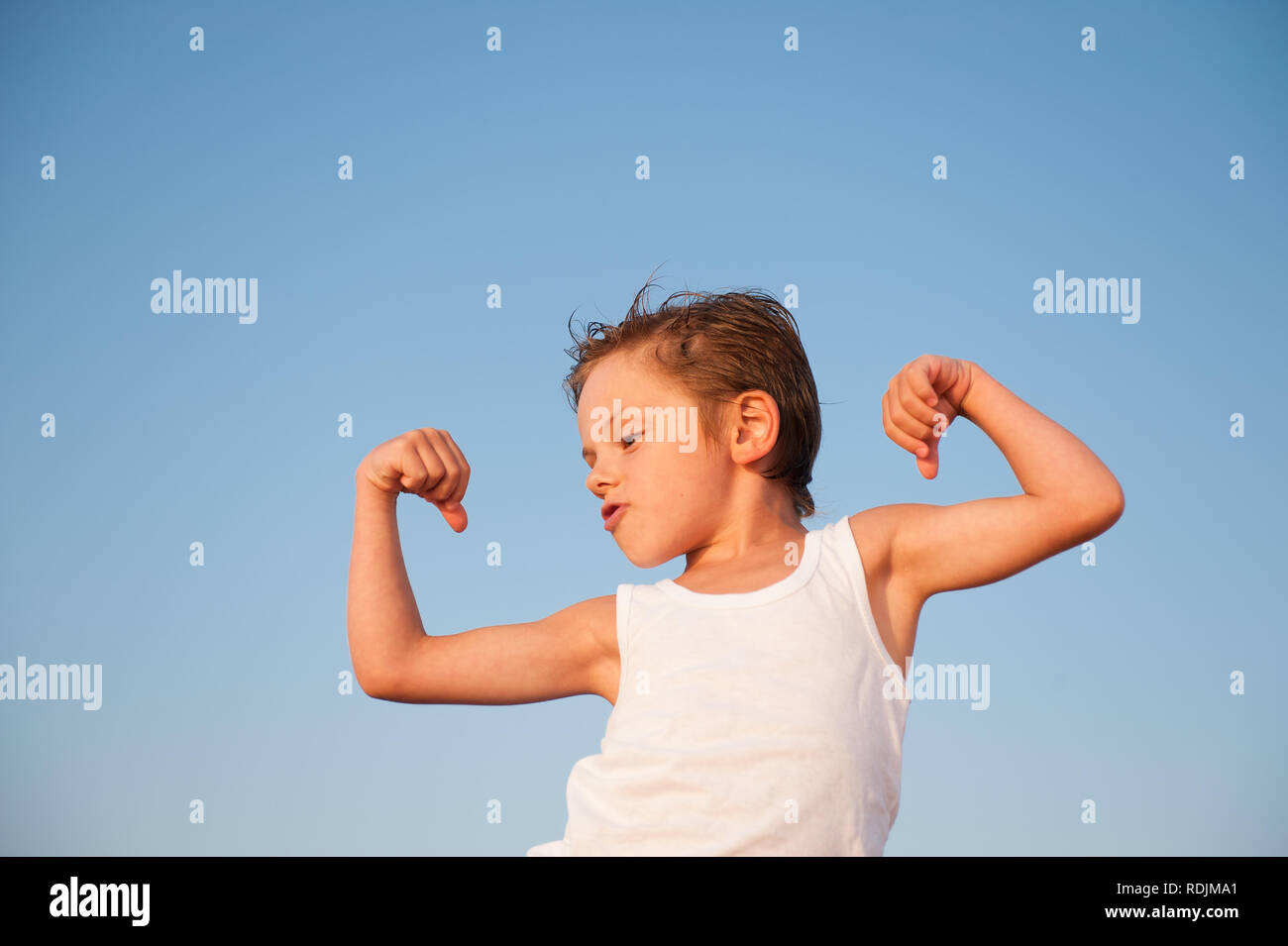 funny little kid showing his muscles on blue sky background with copy ...