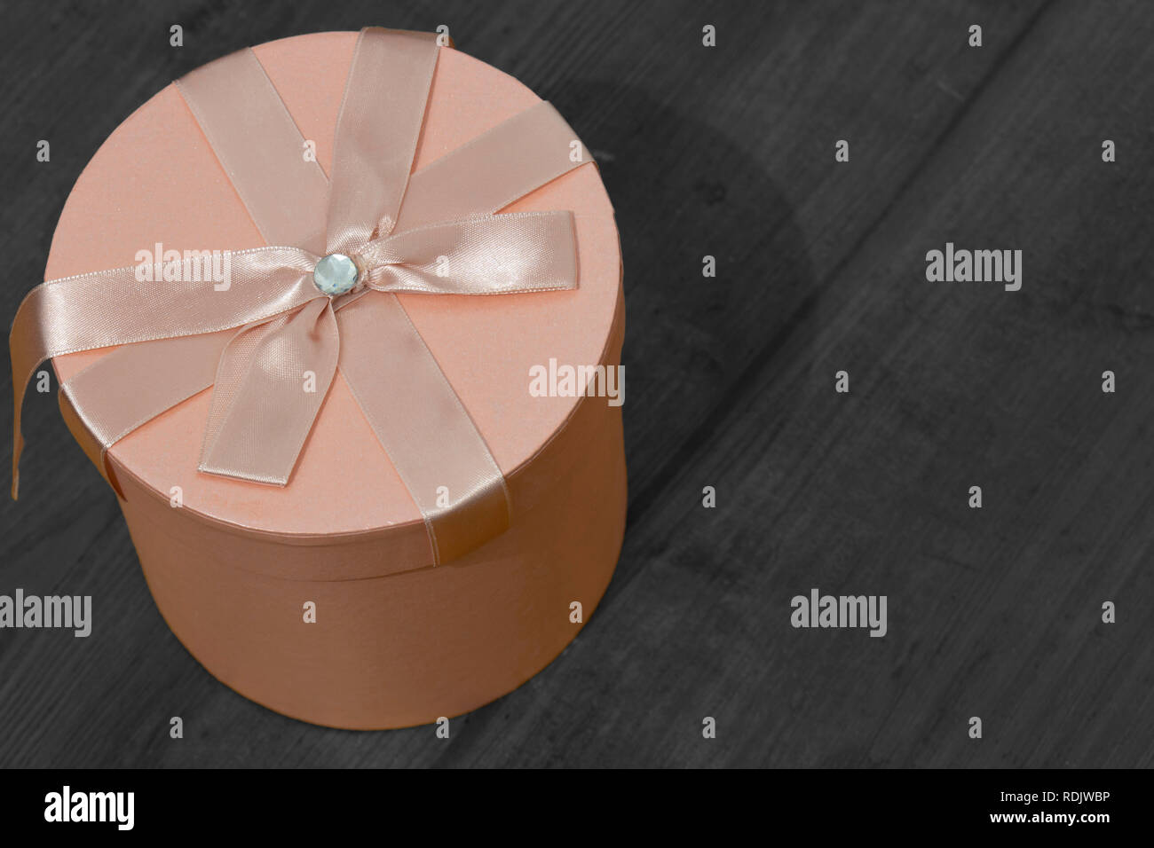 Gift box in pink coral with a ribbon and jewel on a wooden background ...